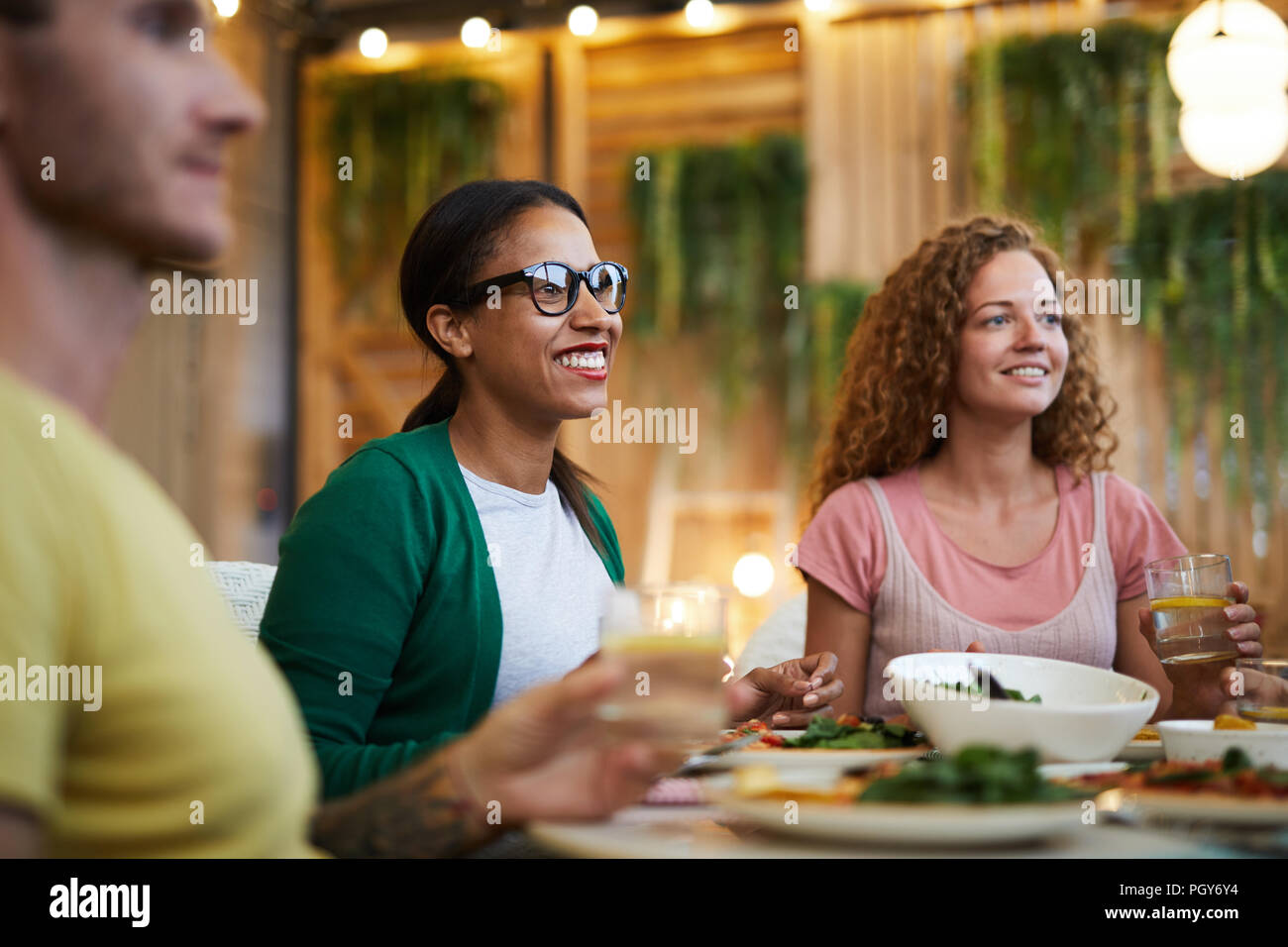Two happy intercultural girls sitting by served festive table at dinner ...