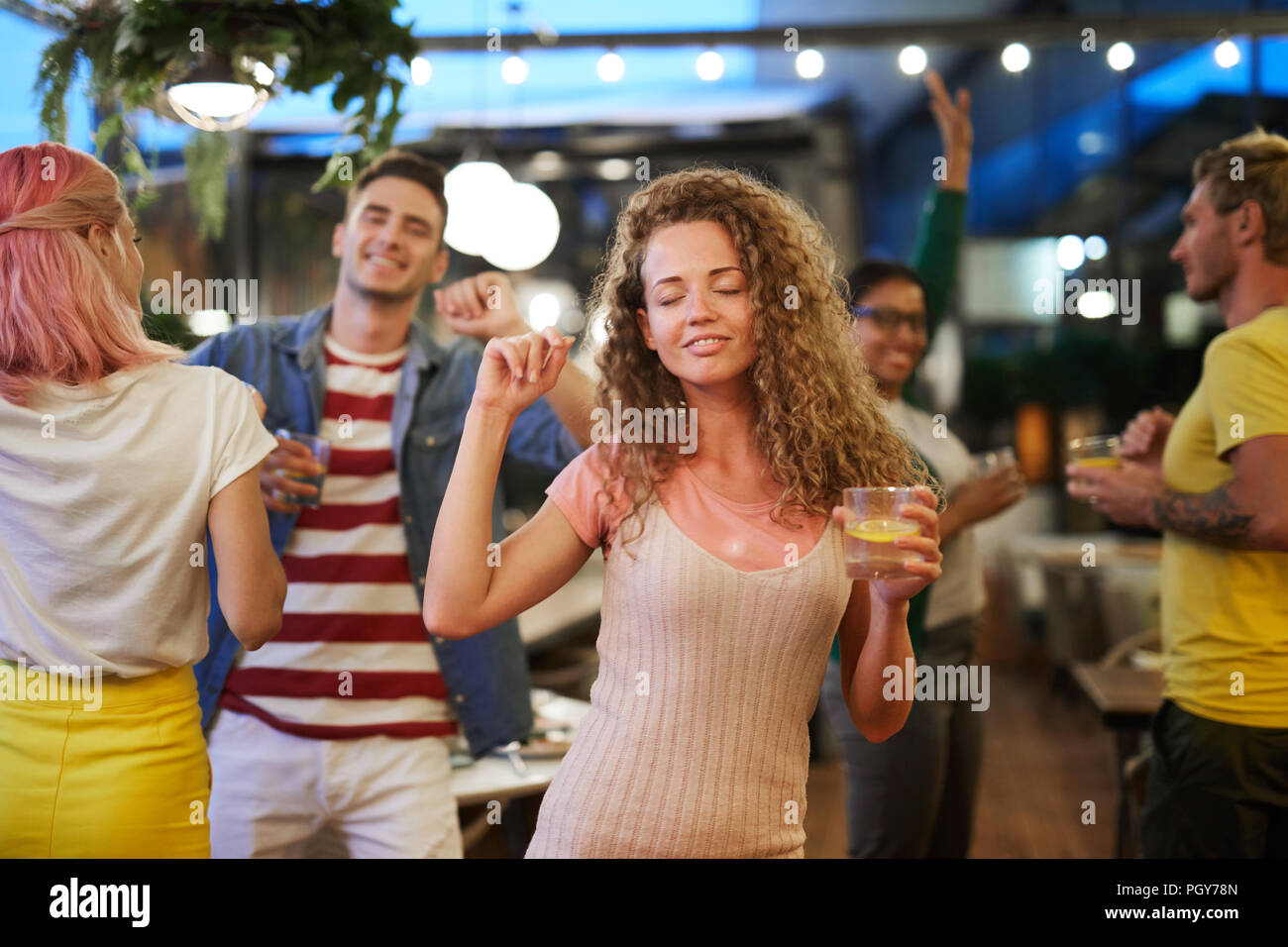 Young excited woman with drink enjoying dancing alone among her friends ...