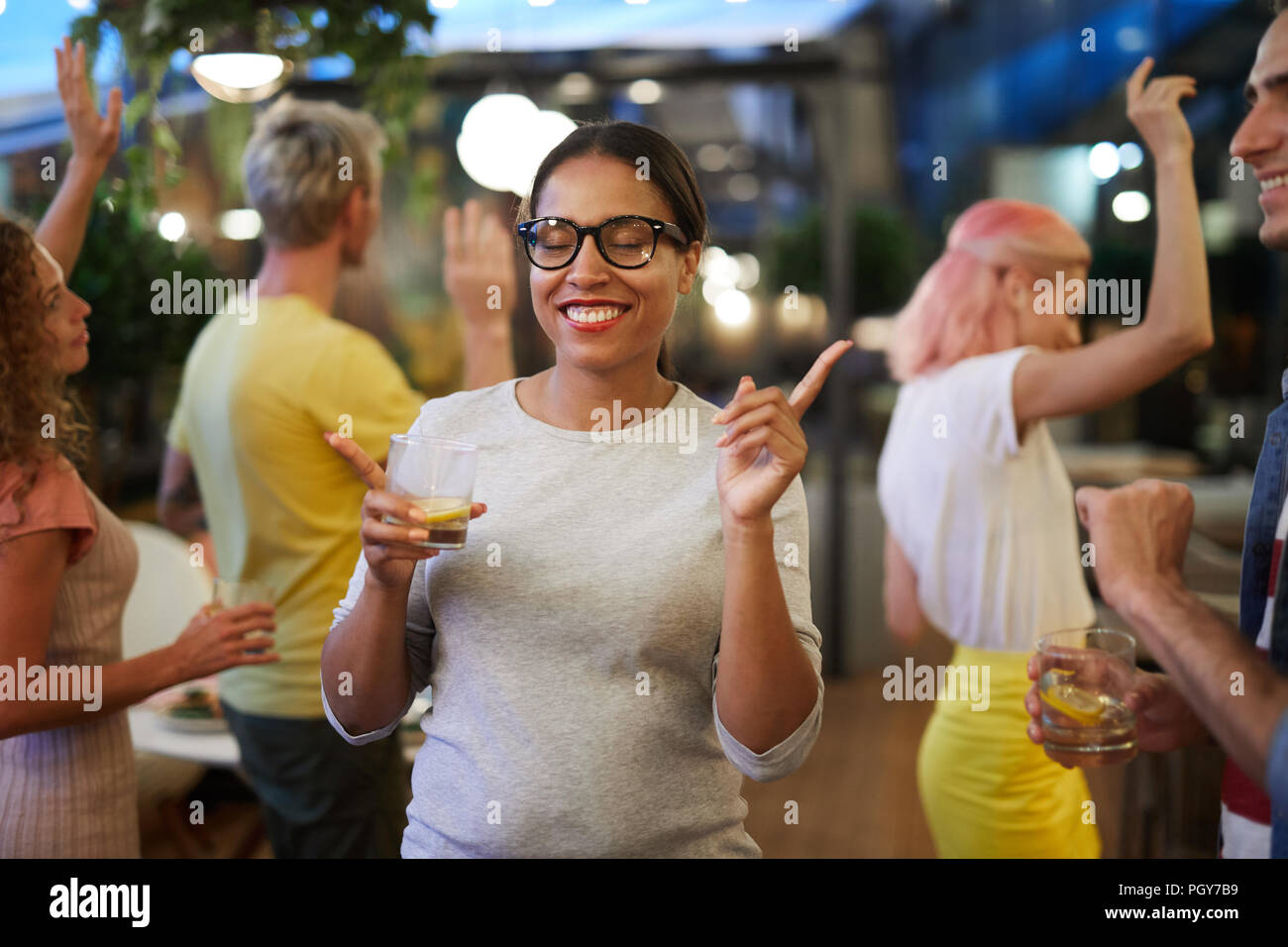 Young ecstatic female with glass of lemonade dancing at party with ...