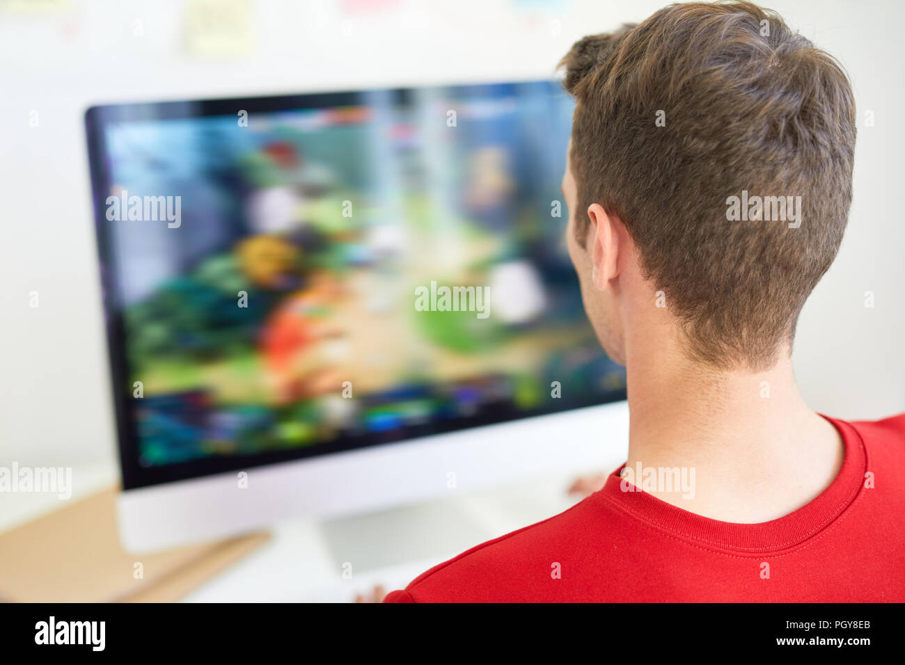 Back view of young designer in front of computer screen in moment of ...