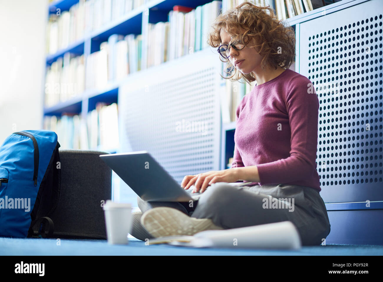 Confident female student using wifi while sitting on the floor at ...