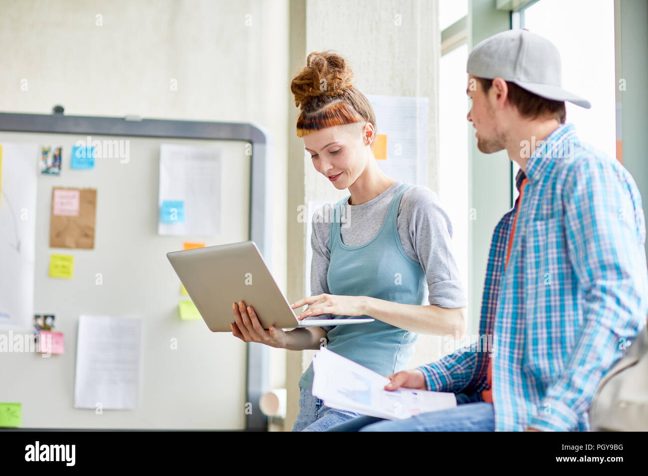 Serious modern students sitting on window sill and using laptop while ...