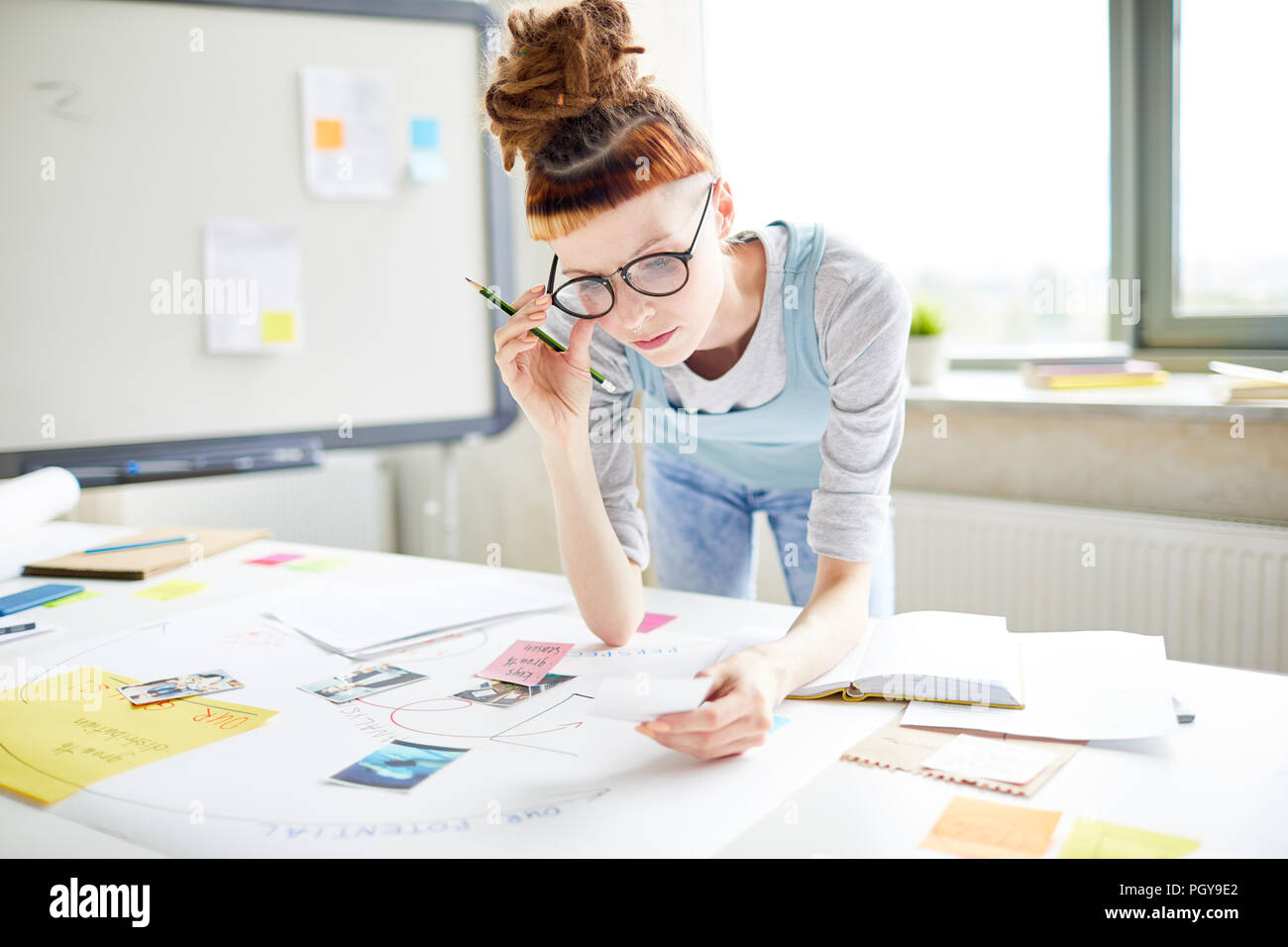 Serious thoughtful female hipster marketer adjusting glasses while ...
