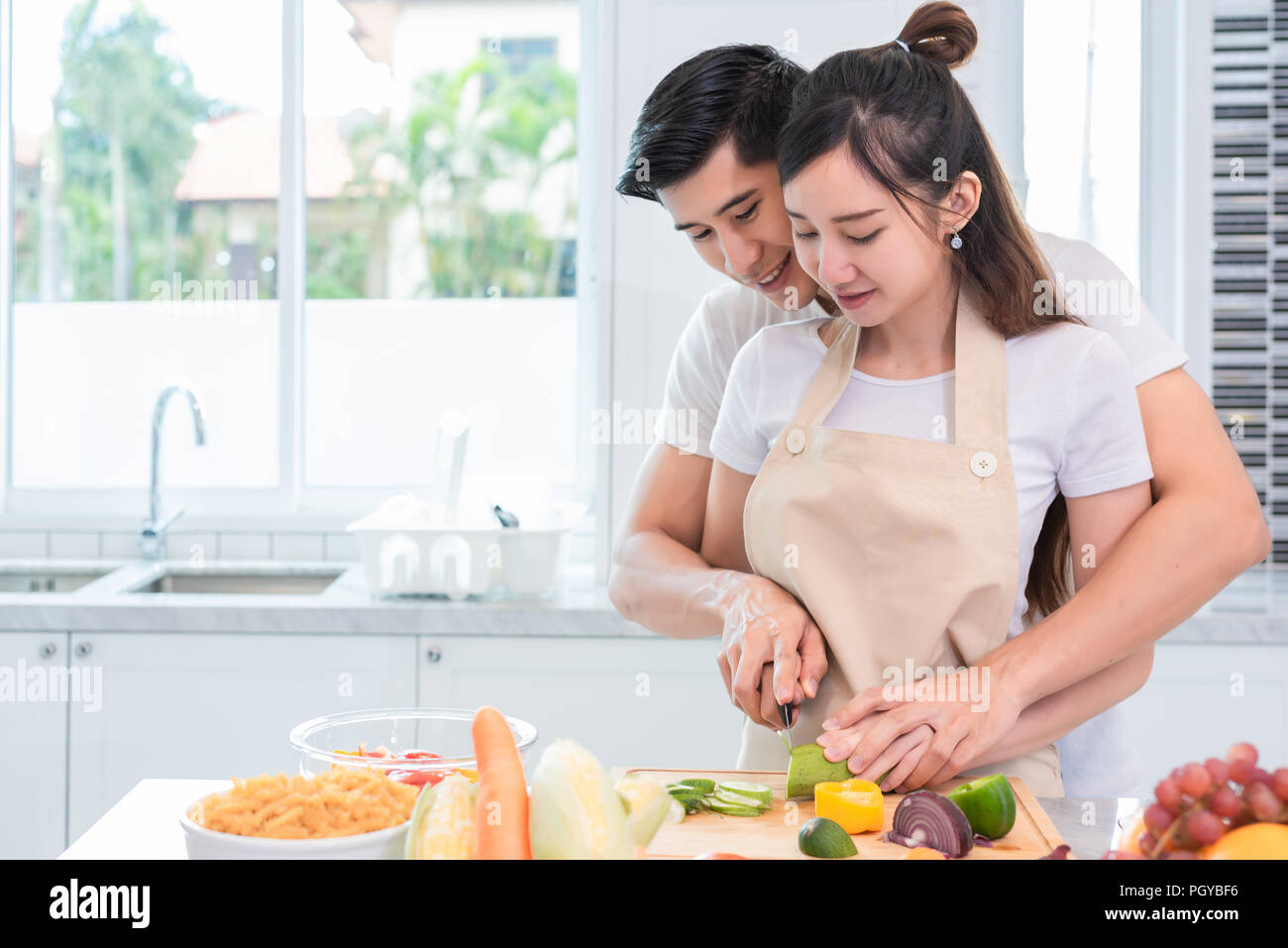 Asian couples cooking and slicing vegetable in kitchen together. Man ...
