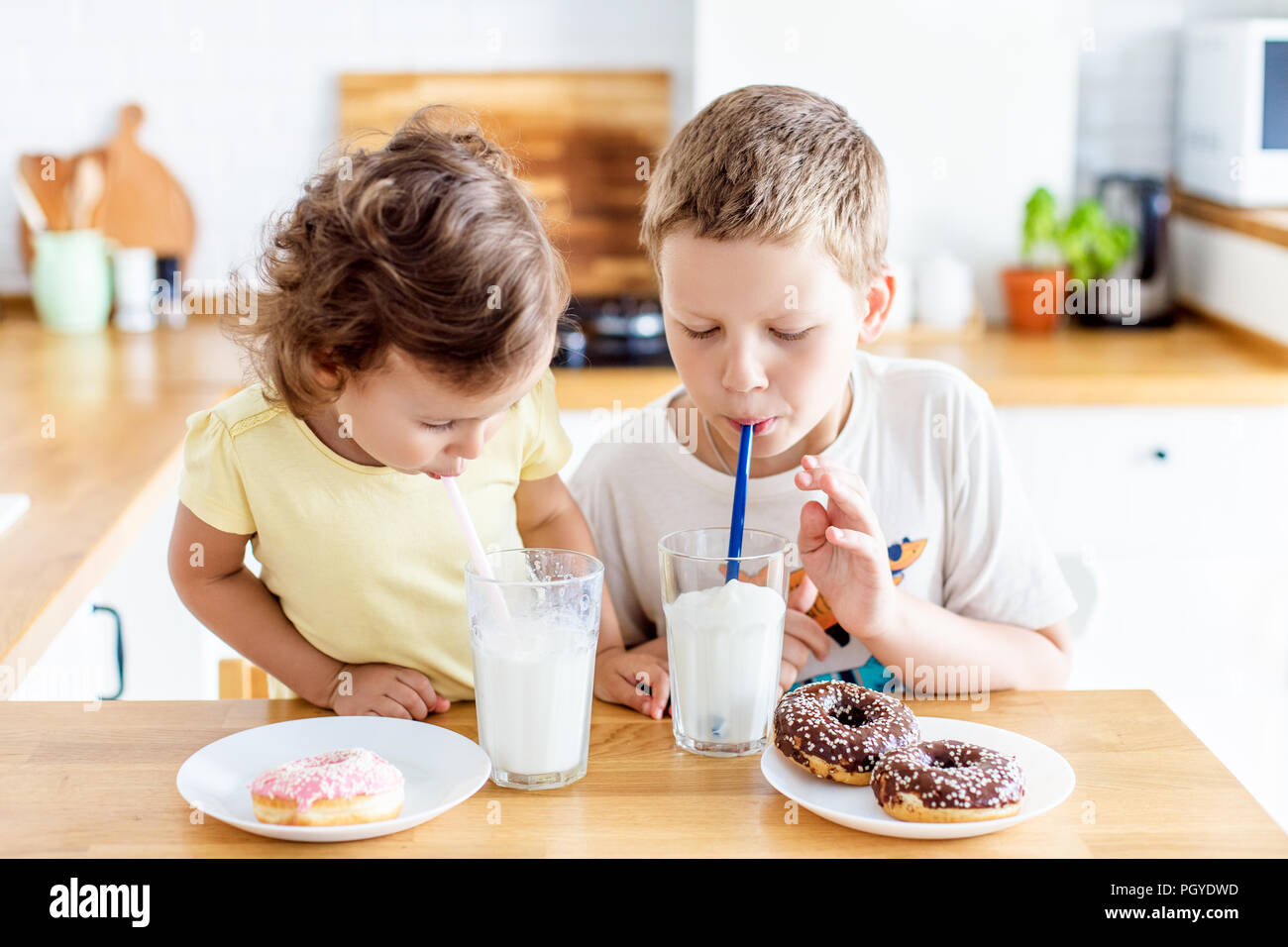 Children eating donuts and drinking milk on the white kitchen at home ...