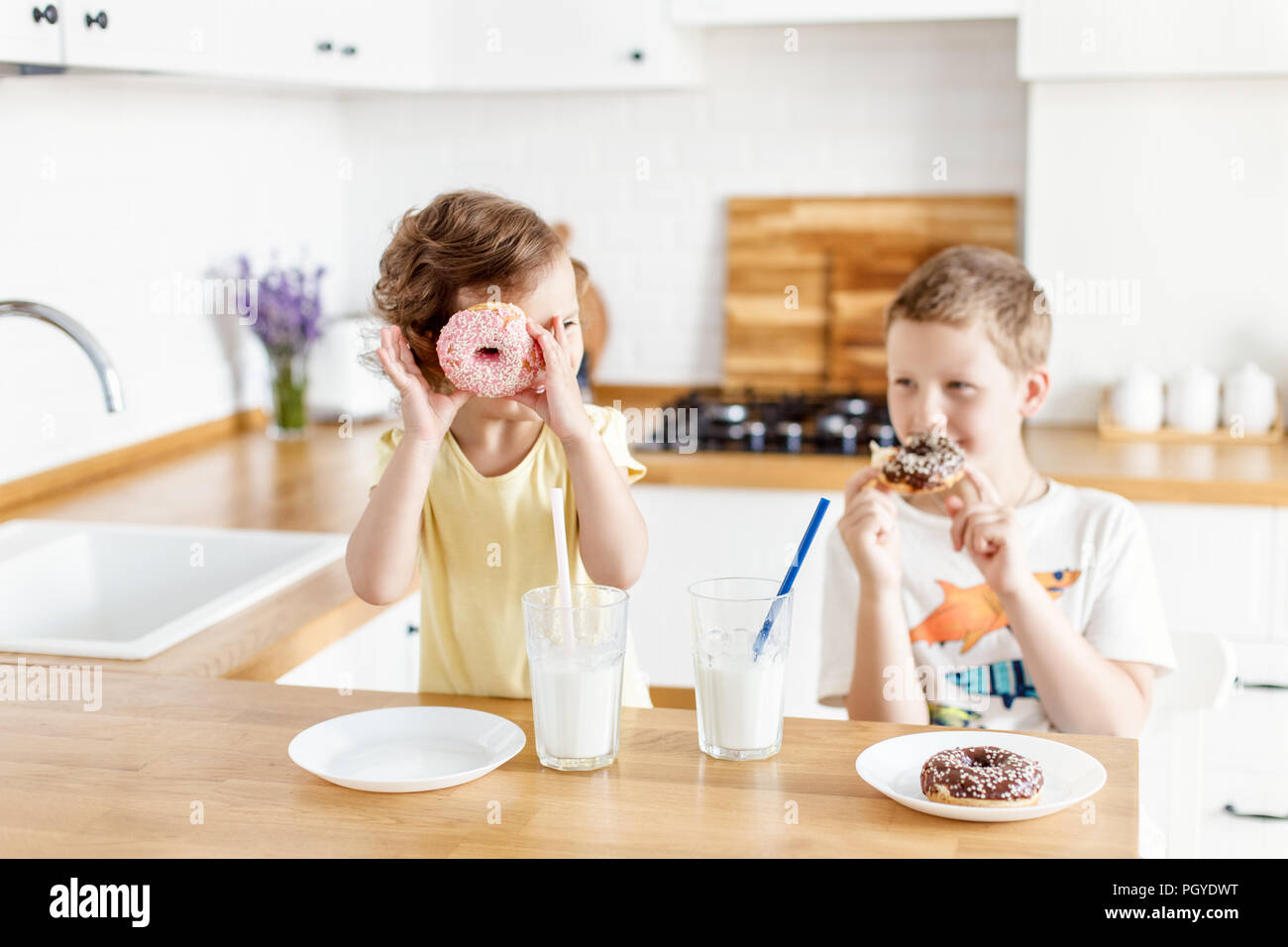 Children eating donuts and drinking milk on the white kitchen at home ...