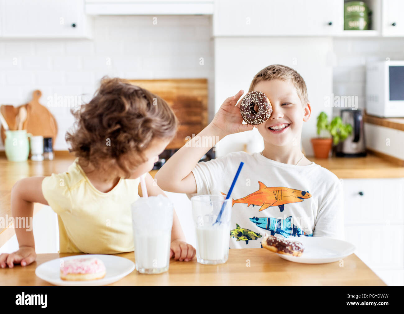 Children eating donuts and drinking milk on the white kitchen at home ...