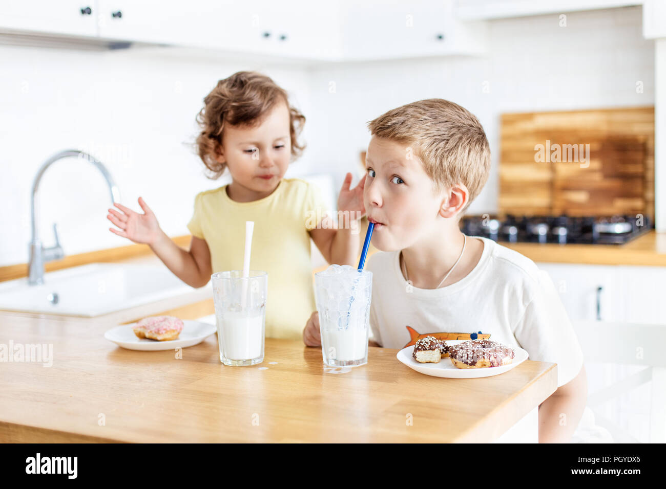 Children eating donuts and drinking milk on the white kitchen at home ...