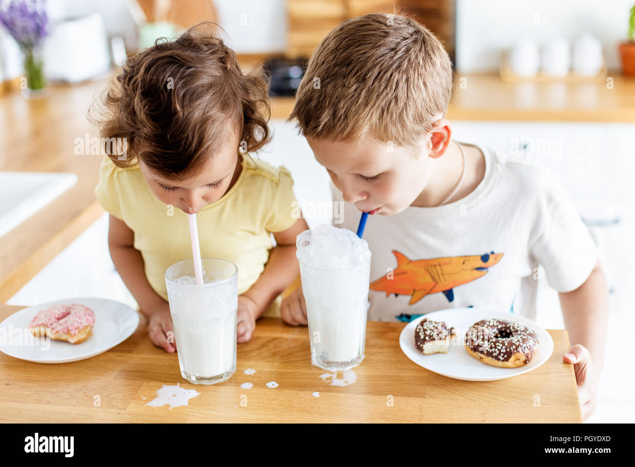 Children eating donuts and drinking milk on the white kitchen at home ...