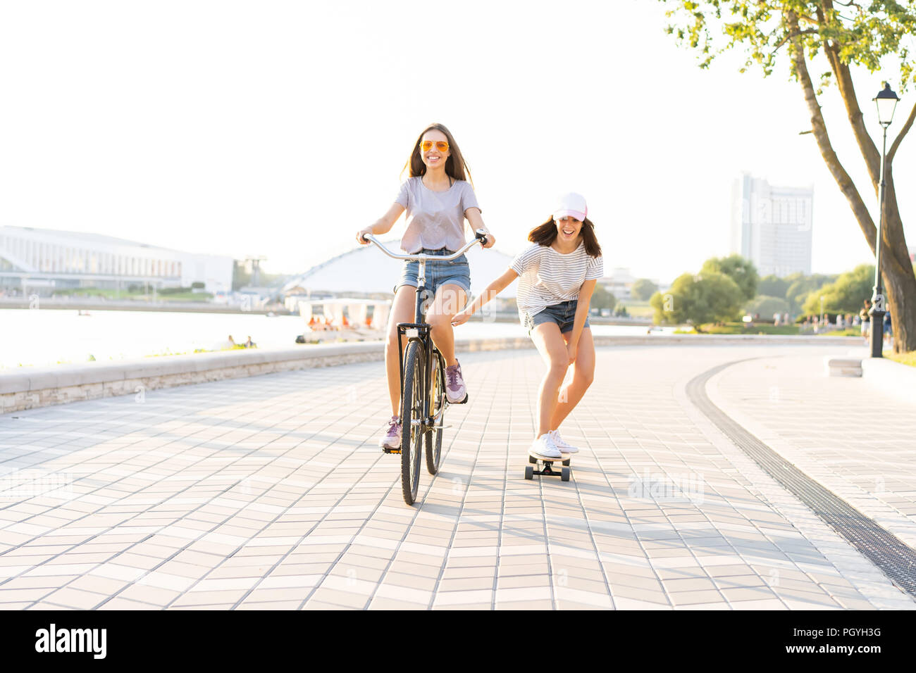 Cute laughing young woman in jeans shorts on bike pulling girl holding ...