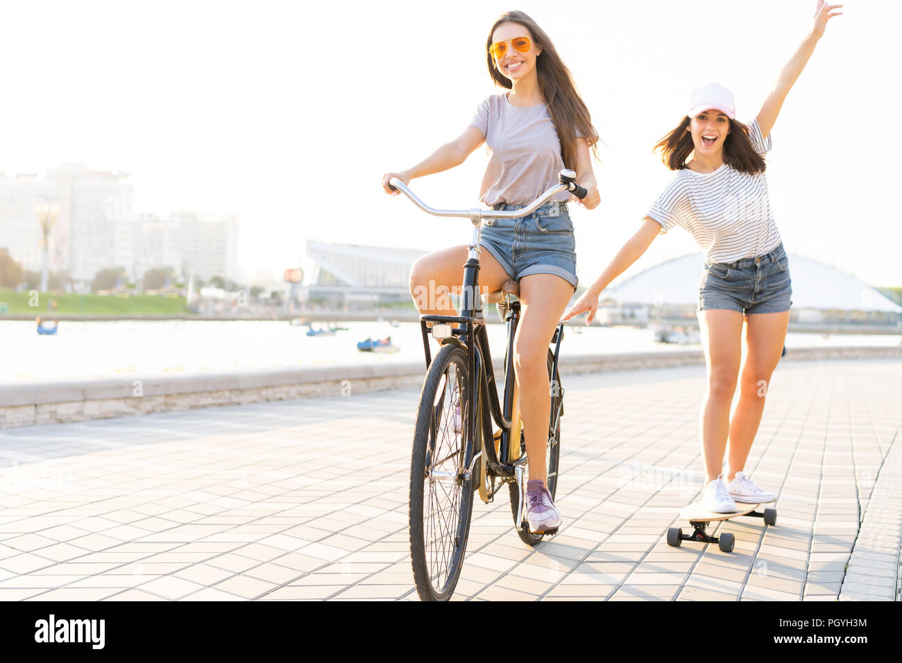 Cute laughing young woman in jeans shorts on bike pulling girl holding ...