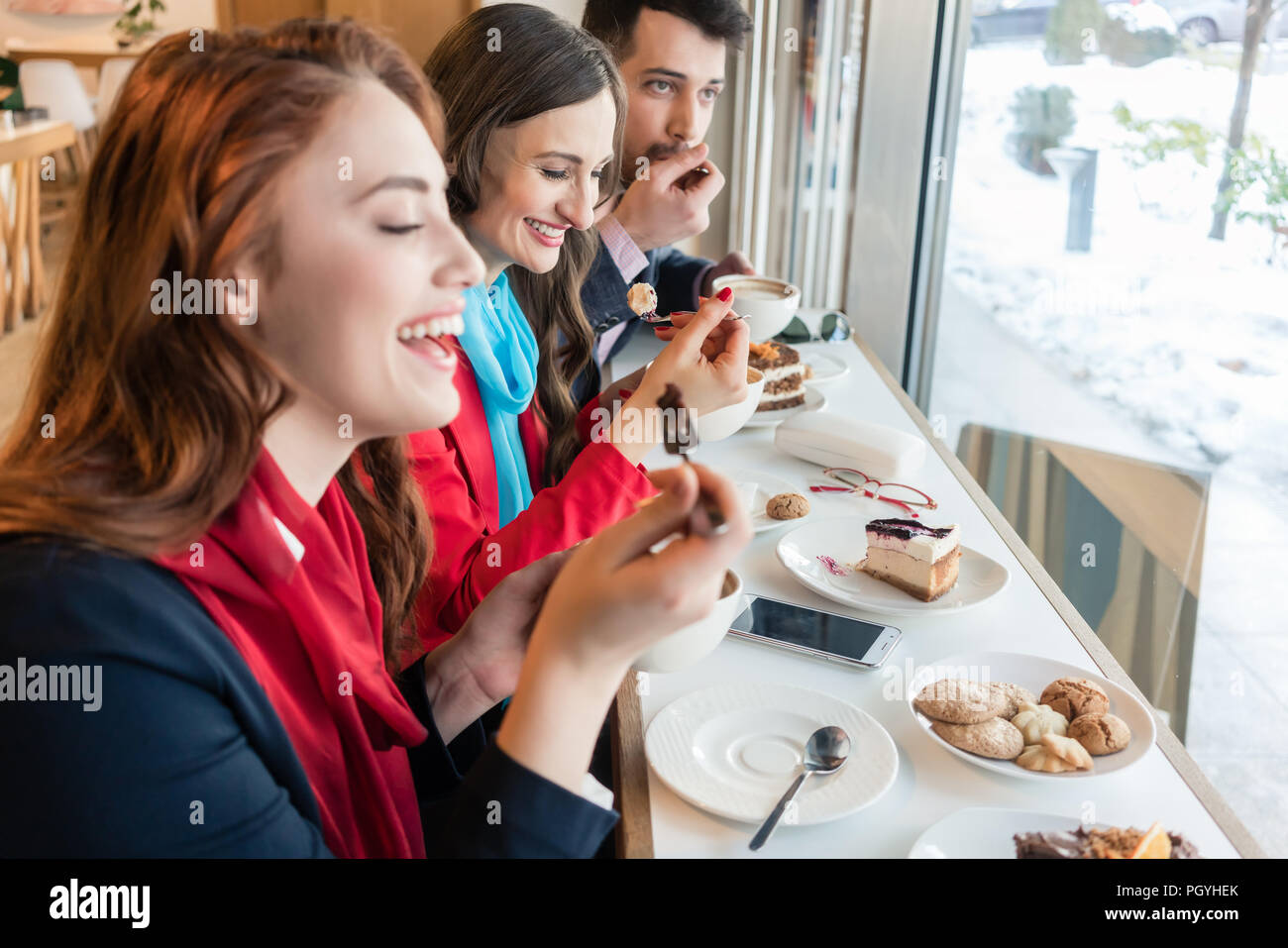 Side view of three young colleagues smiling happy while eating ...