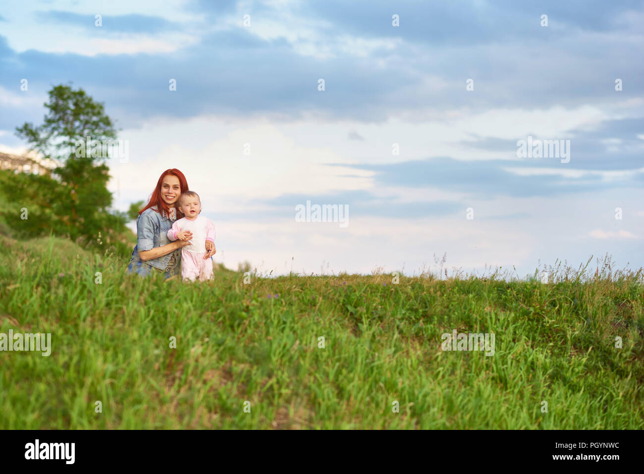 Young mother hugging cute little daughter sitting on green grass in ...