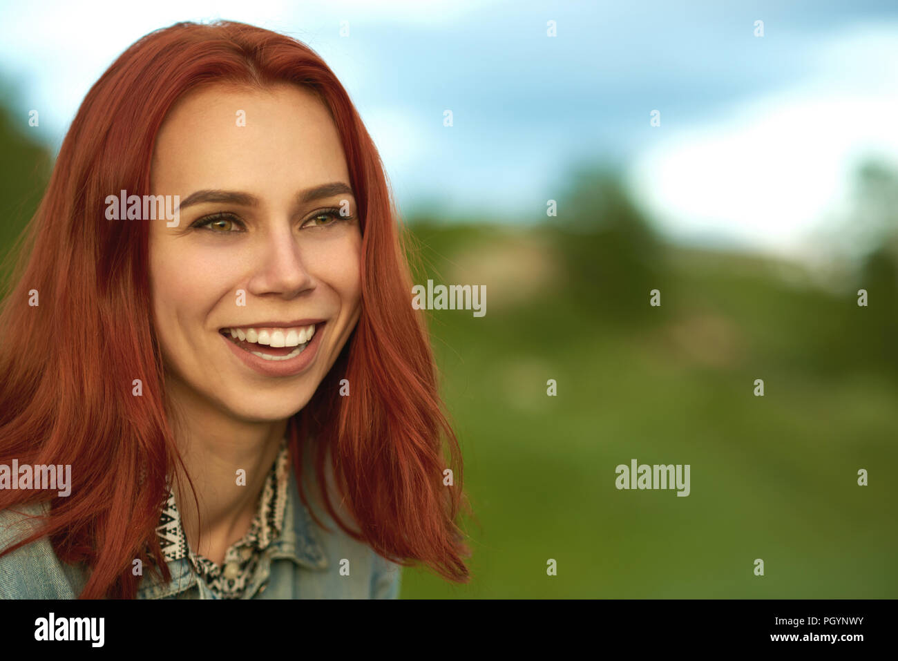 Laughing woman with short red hair posing on green field during sunny ...
