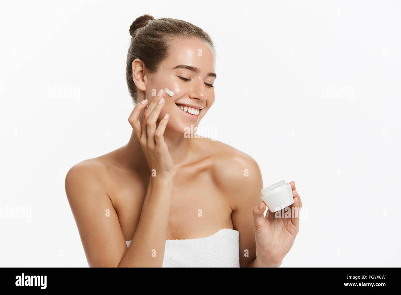 Beautiful young woman applying cosmetic cream treatment on her face isolated on white background ...