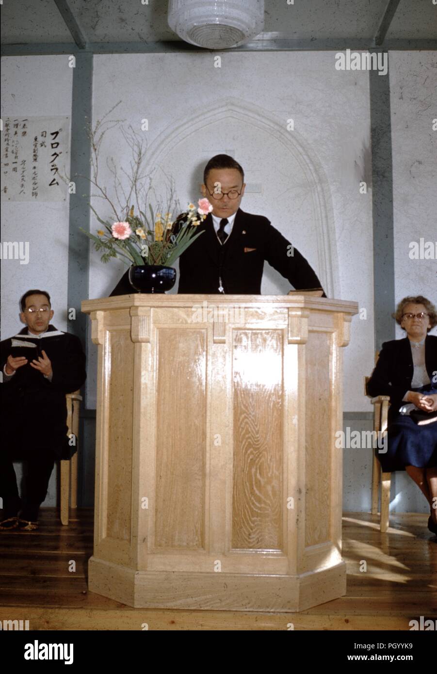 A Japanese man stands at an altar and preaches at a Christian ...