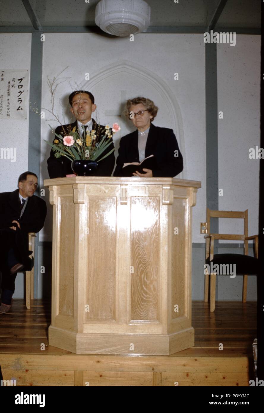 A female Caucasian missionary and a Japanese man stand and preach ...