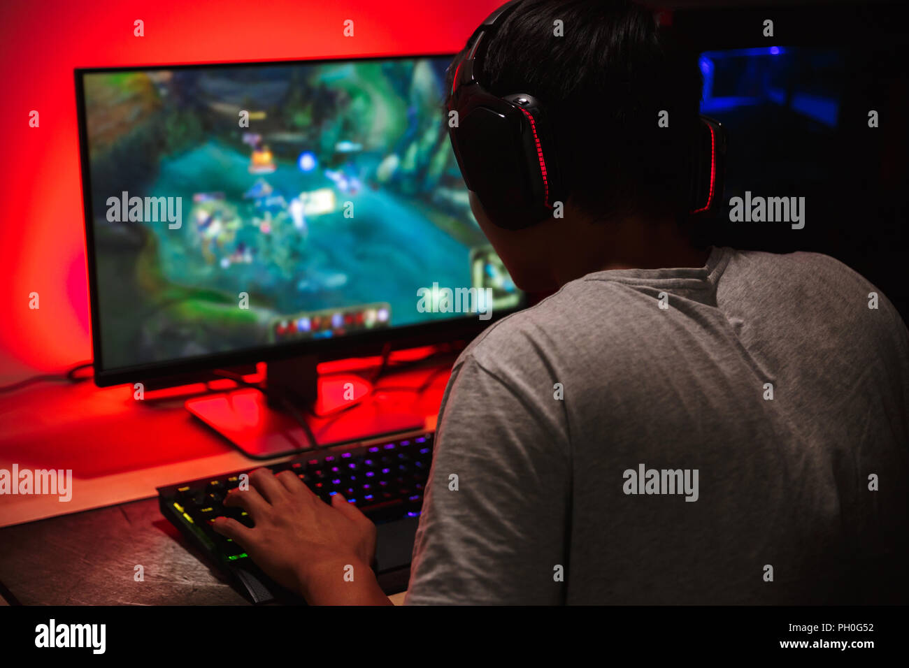 Teenage gamer boy playing video games on computer in dark room wearing ...