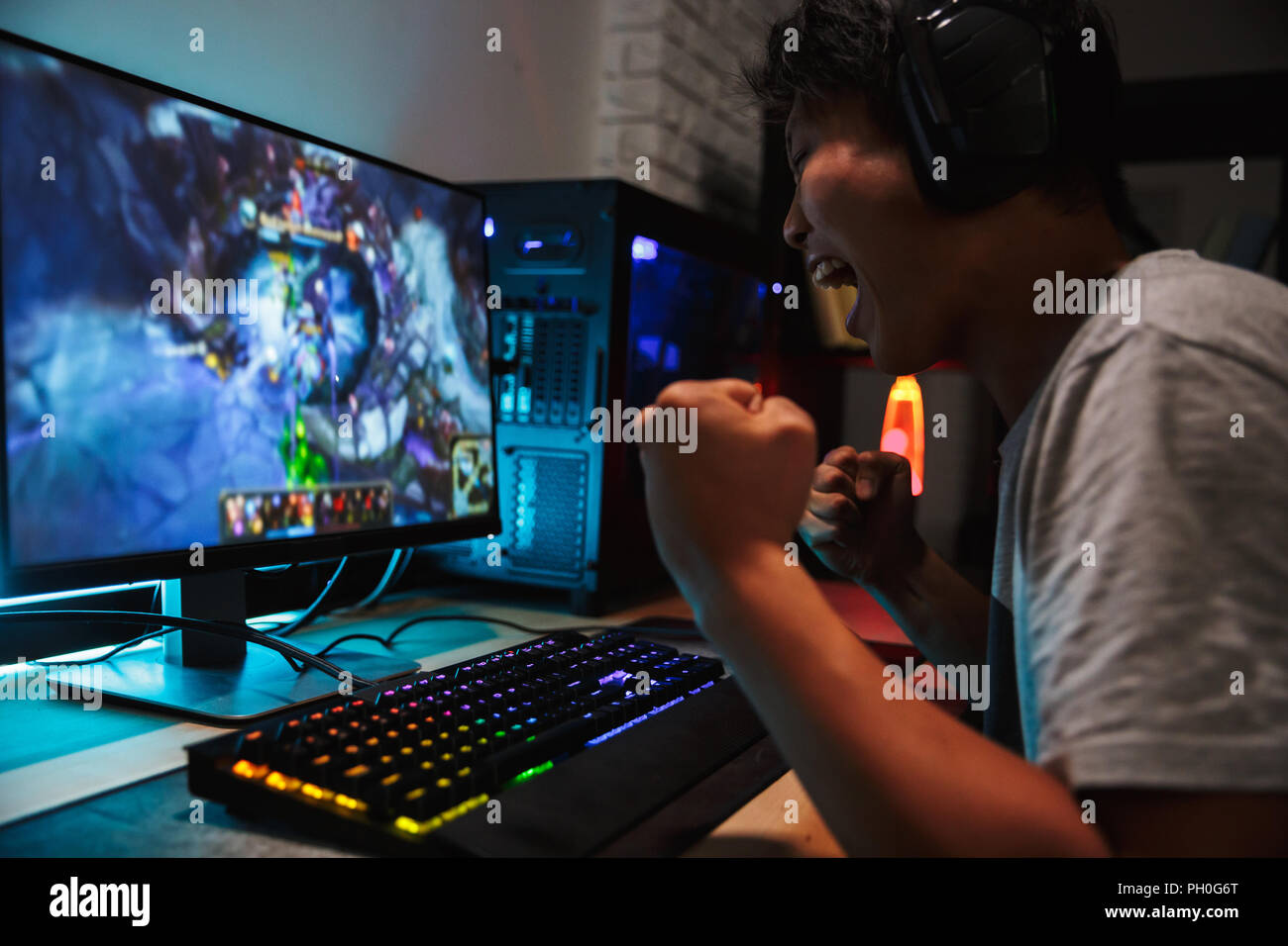 Joyful asian teen gamer man playing video games on computer in dark ...