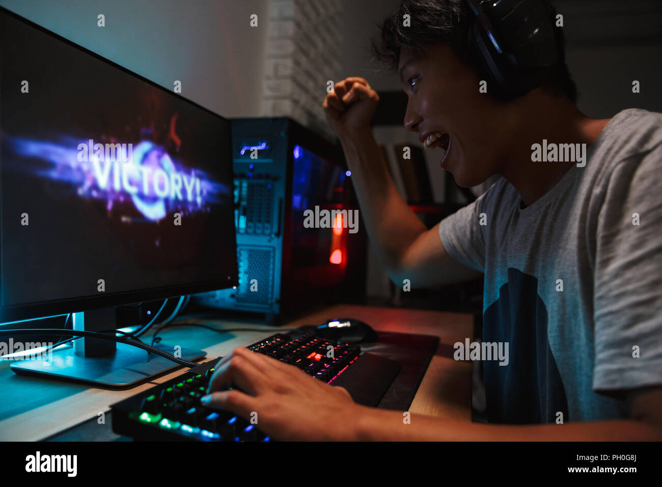 Happy asian gamer boy winning while playing video games on computer in ...