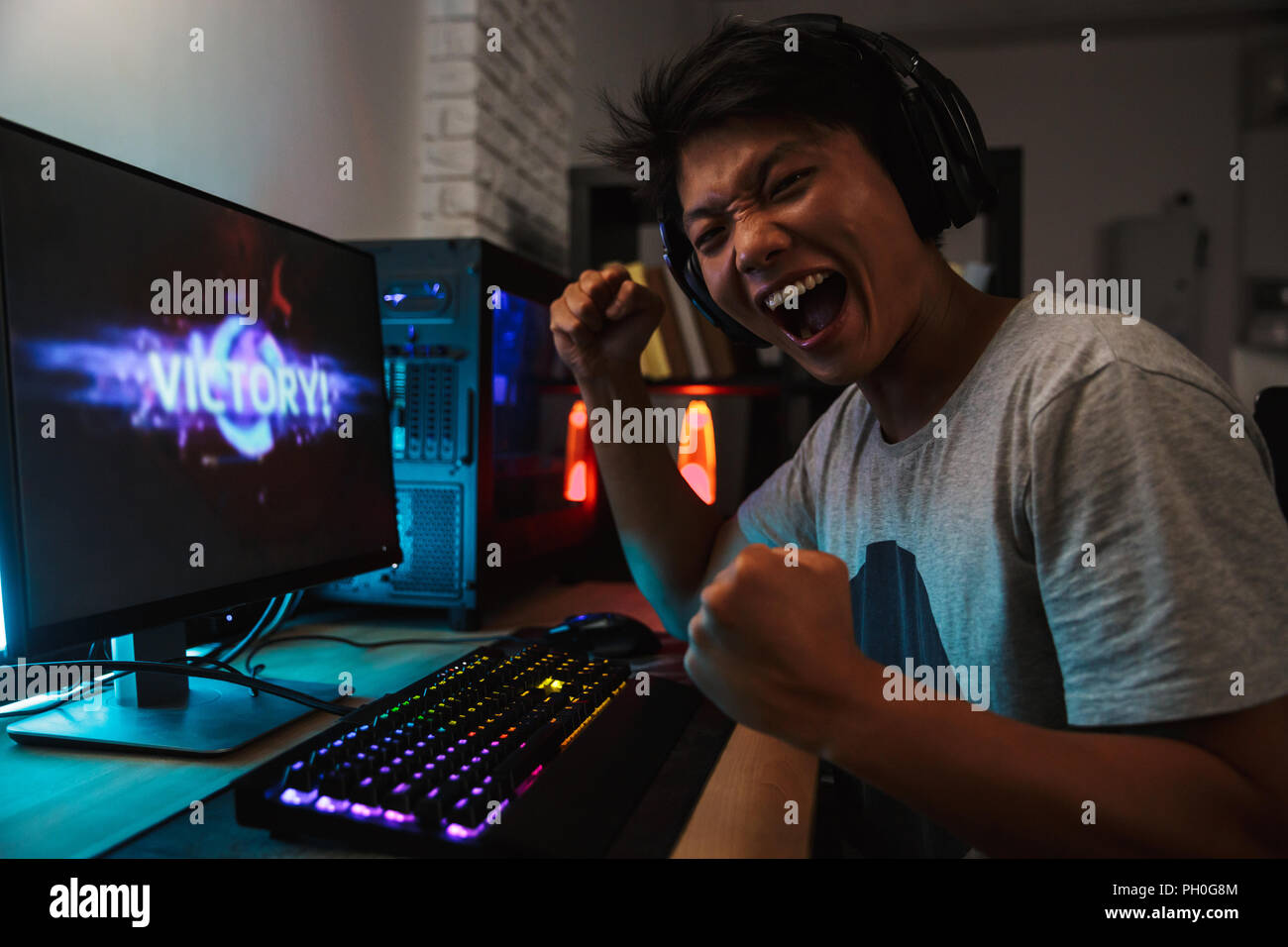 Cheerful asian gamer boy rejoicing victory while playing video games on ...