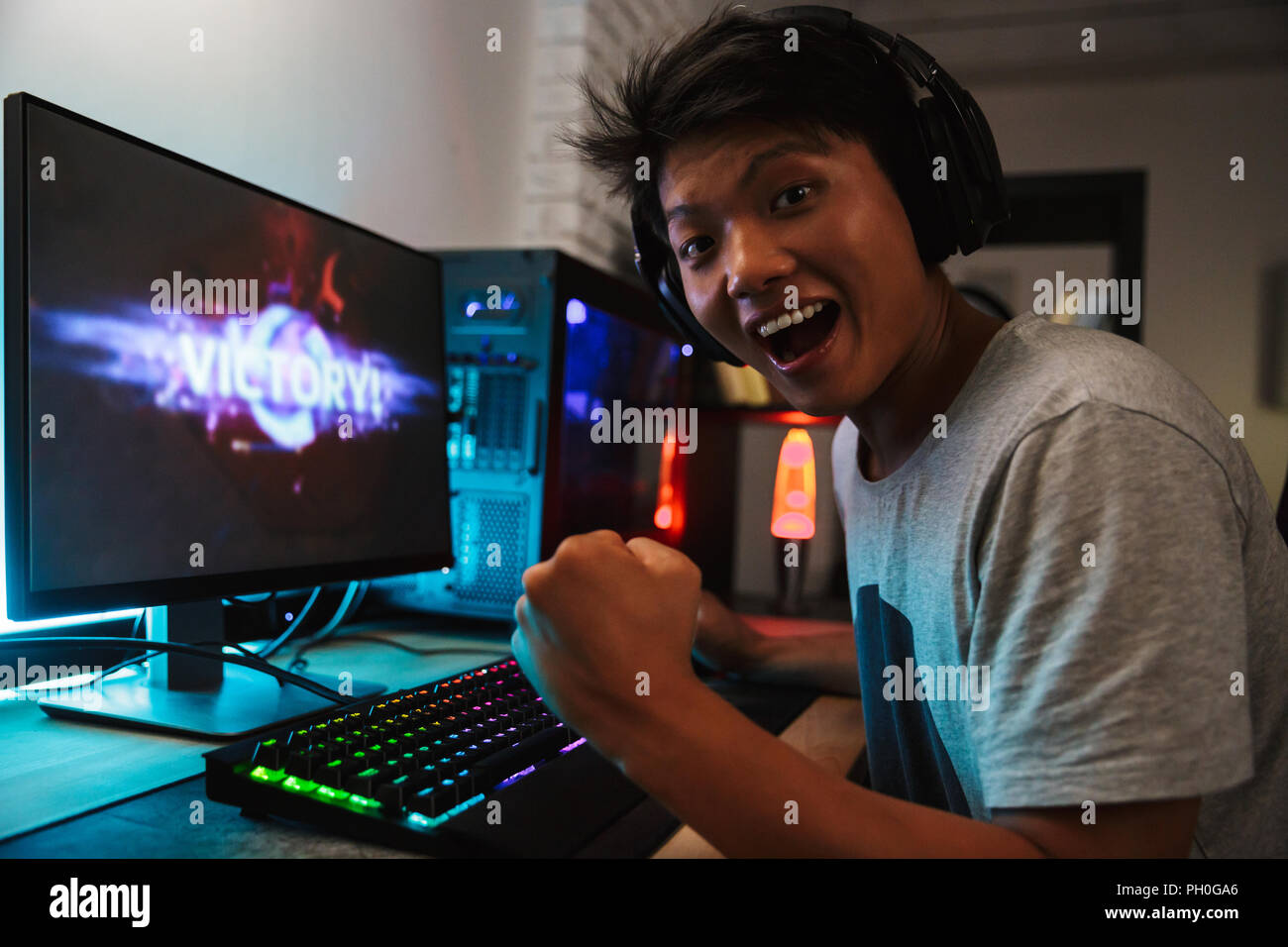 Ecstatic asian gamer boy rejoicing victory while playing video games on ...