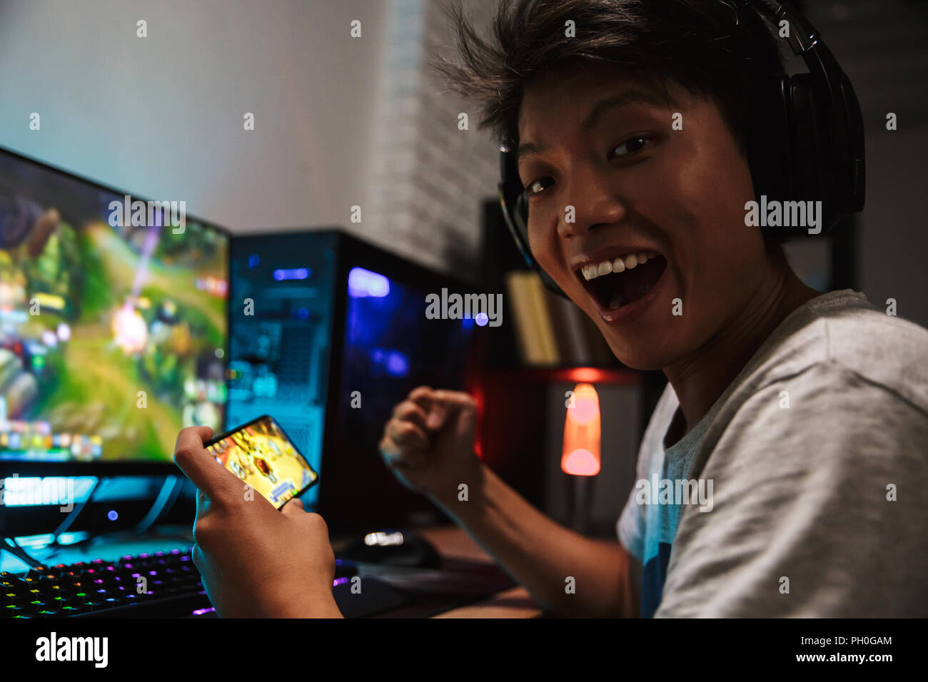 Asian happy gamer boy rejoicing while playing video games on smartphone ...