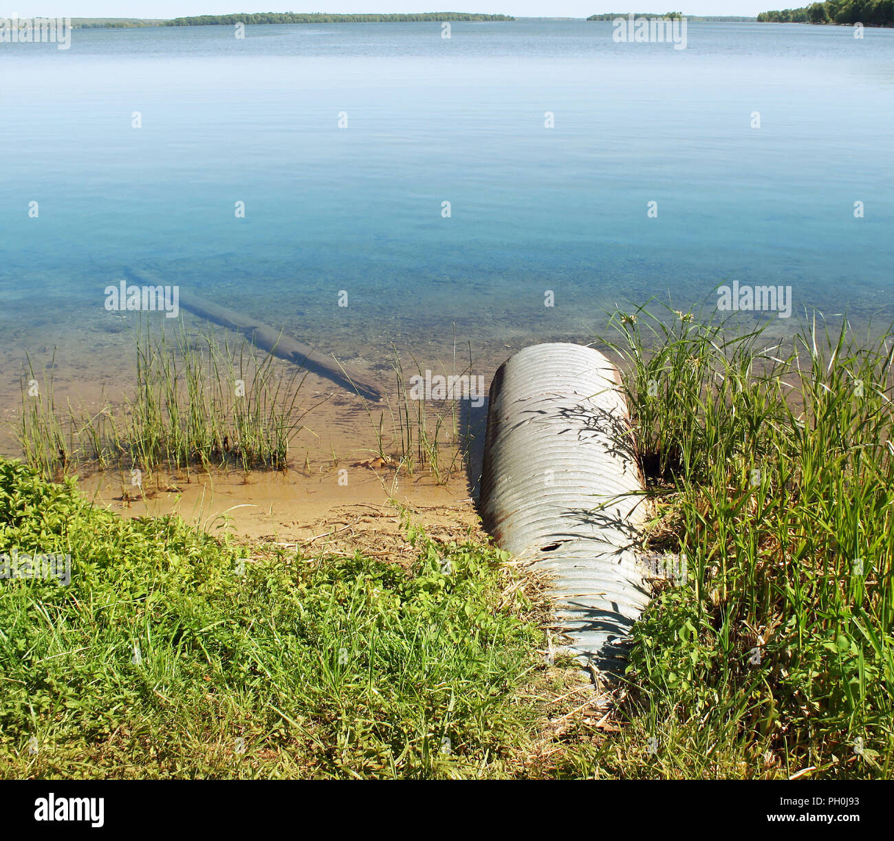 Large metal drain pipe going into a beautiful blue lake Stock Photo - Alamy