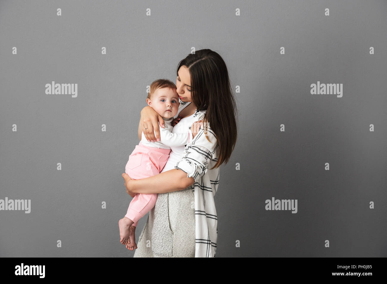 Portrait of a loving young mother holding her little baby girl over gray background Stock Photo ...