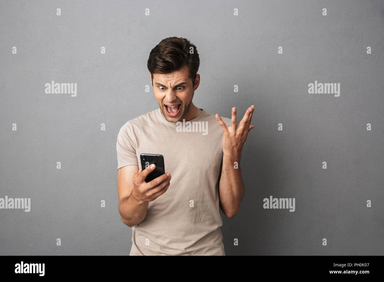 Angry man 20s with short dark hair screaming in rage while holding ...