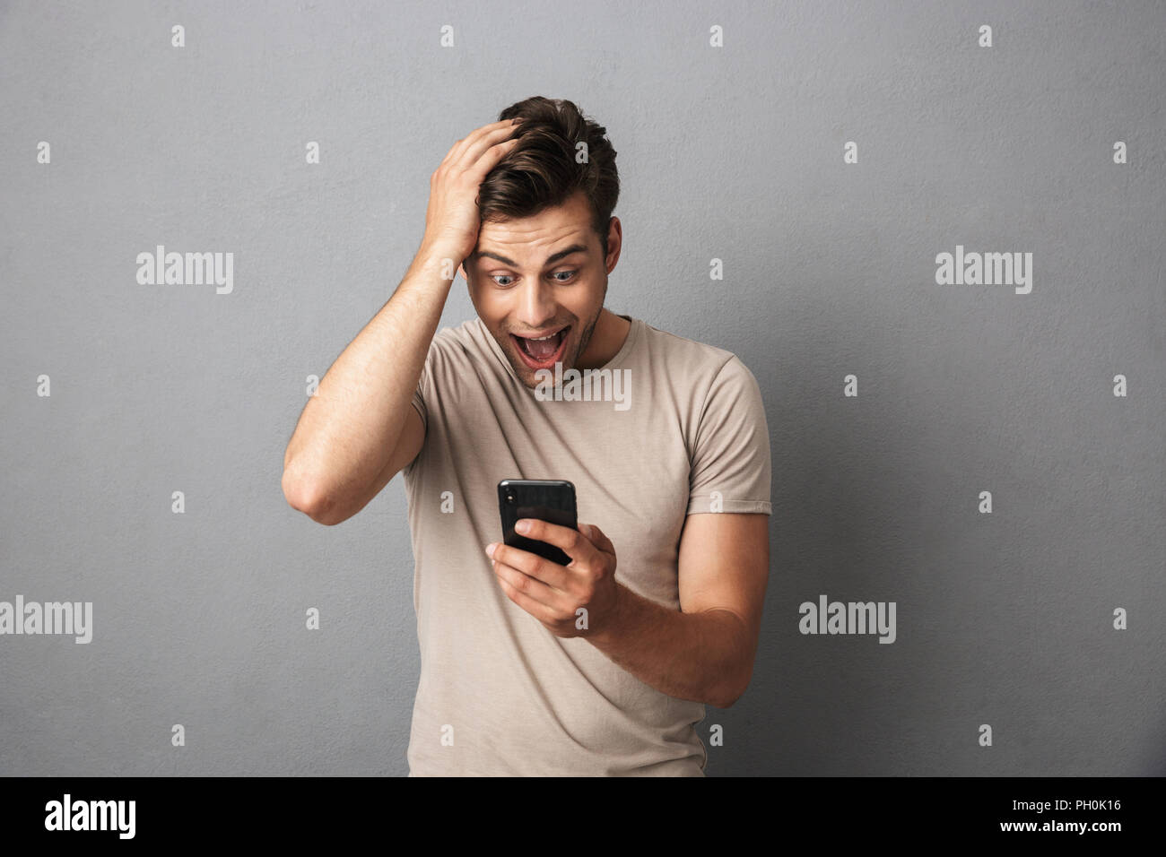 Caucasian young man 20s grabbing head while holding smartphone isolated ...