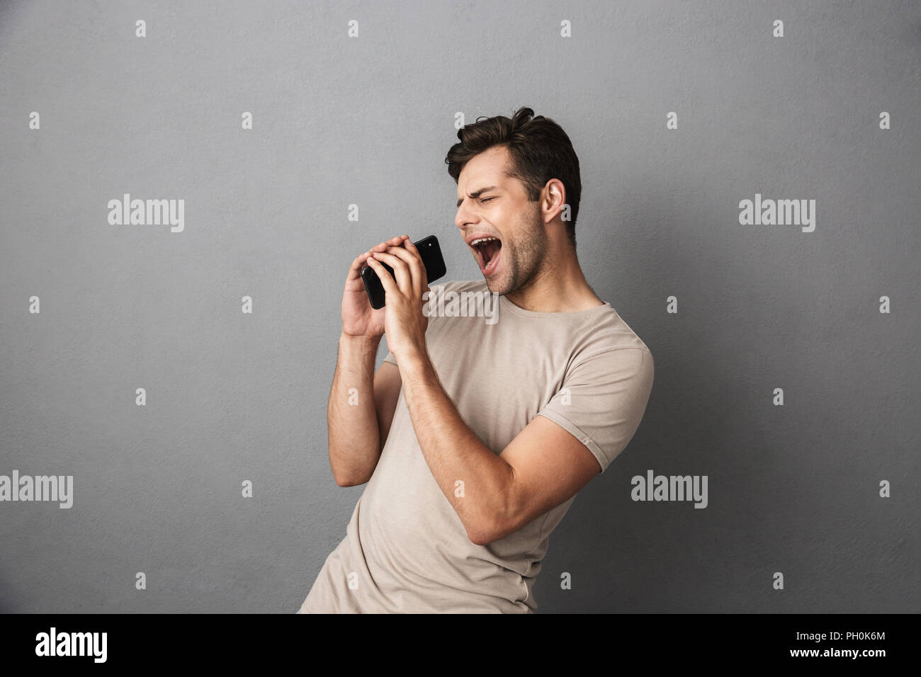 Portrait of a joyful young man in t-shirt isolated over gray backgound ...