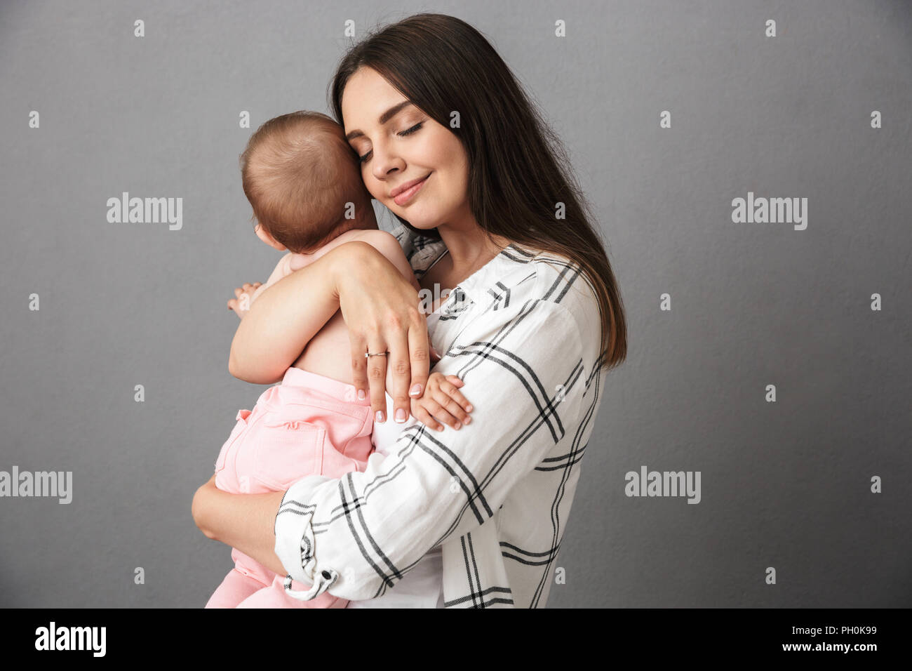 Portrait of a delighted young mother holding her little baby girl over gray background Stock ...