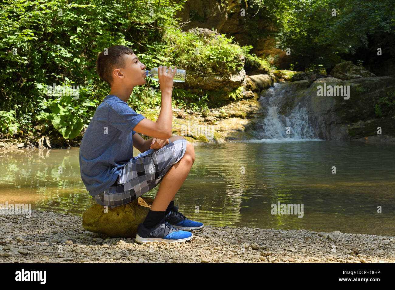 Boy drinks water from bottle outdoors sitting on stone Stock Photo - Alamy