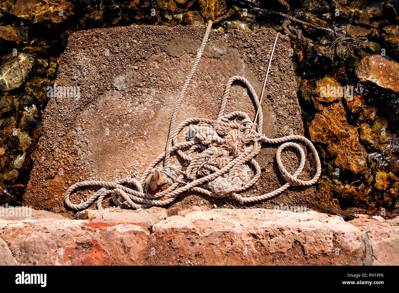 Fishing rope wrinkled and involved left on sunny rock. Cleat and rope ...