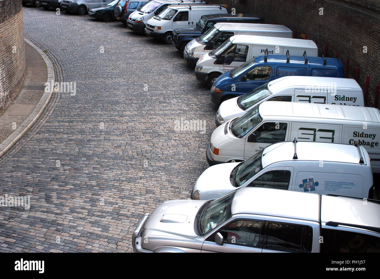 Semi circular row of parked workman's vans all parked in a cobbled ...