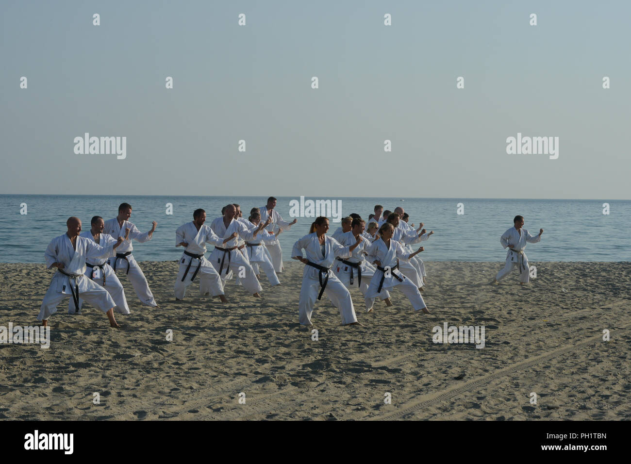 group of shotokan karatekas practicing at the beach in the morning sun ...