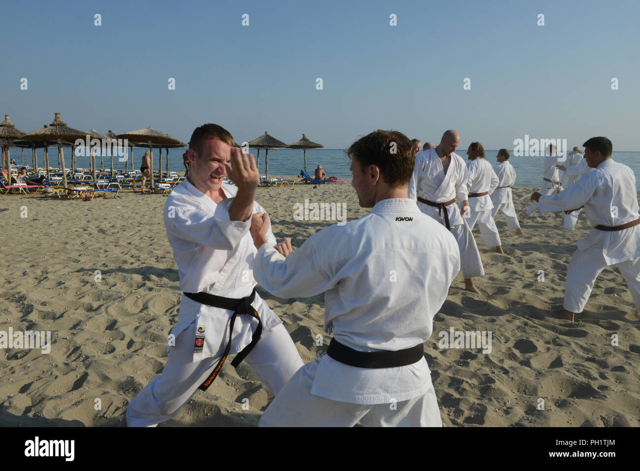 group of shotokan karatekas practicing at the beach in the morning sun ...