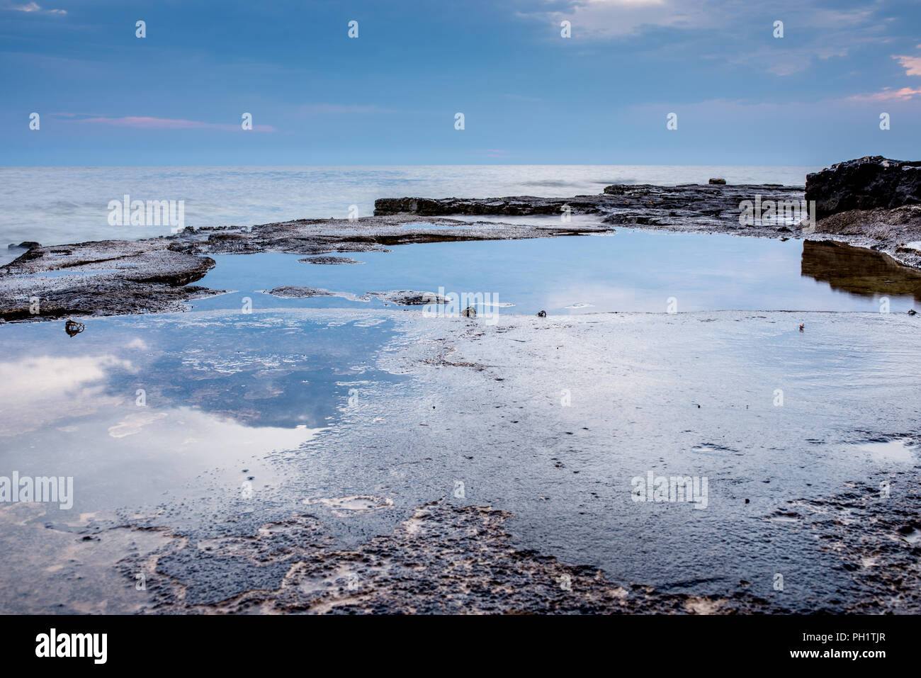 Tranquil rock pool overlooking the ocean reflecting the sunny blue sky ...