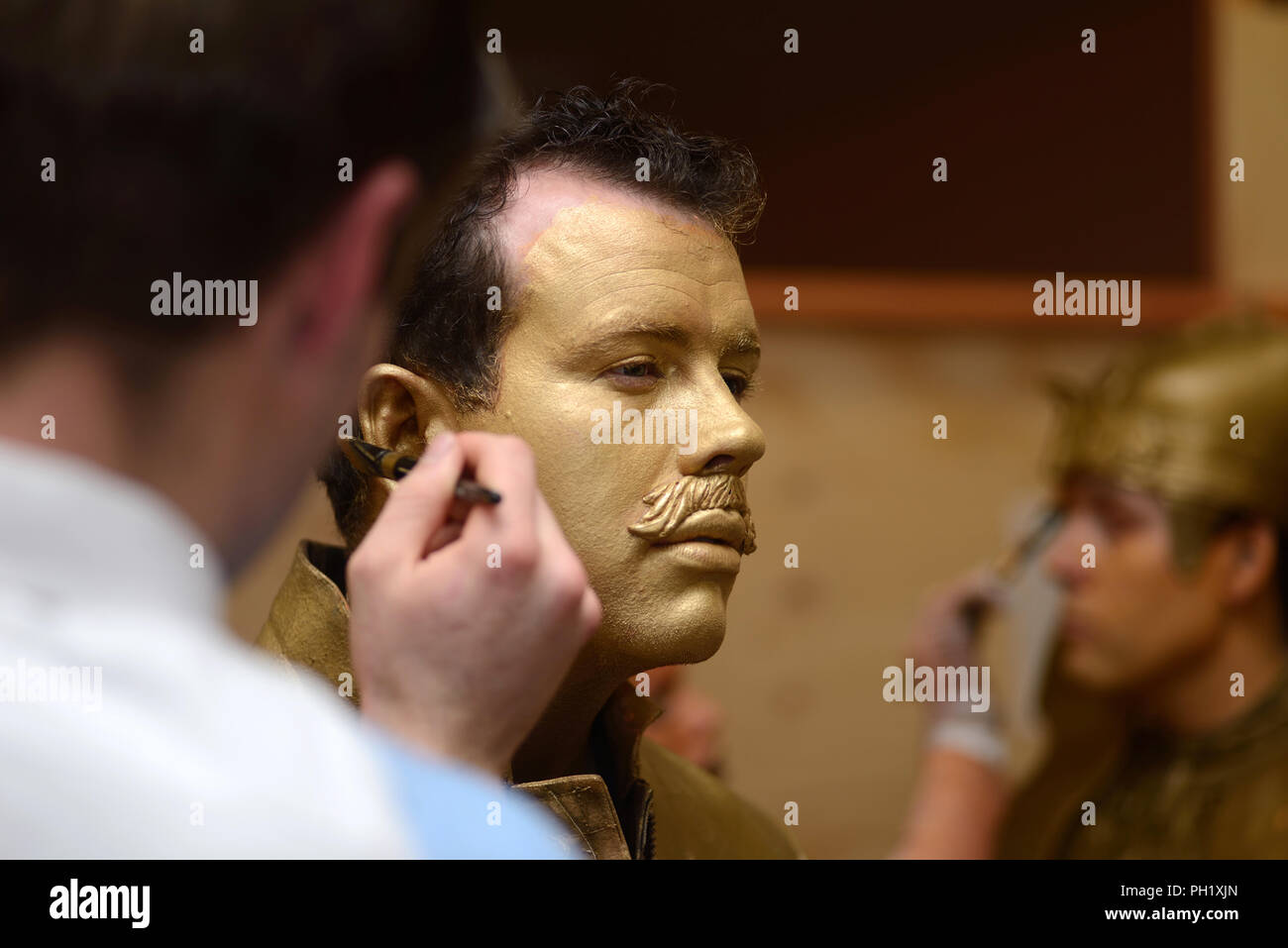 A make-up artist applies gold paint to an actor's face before a ...