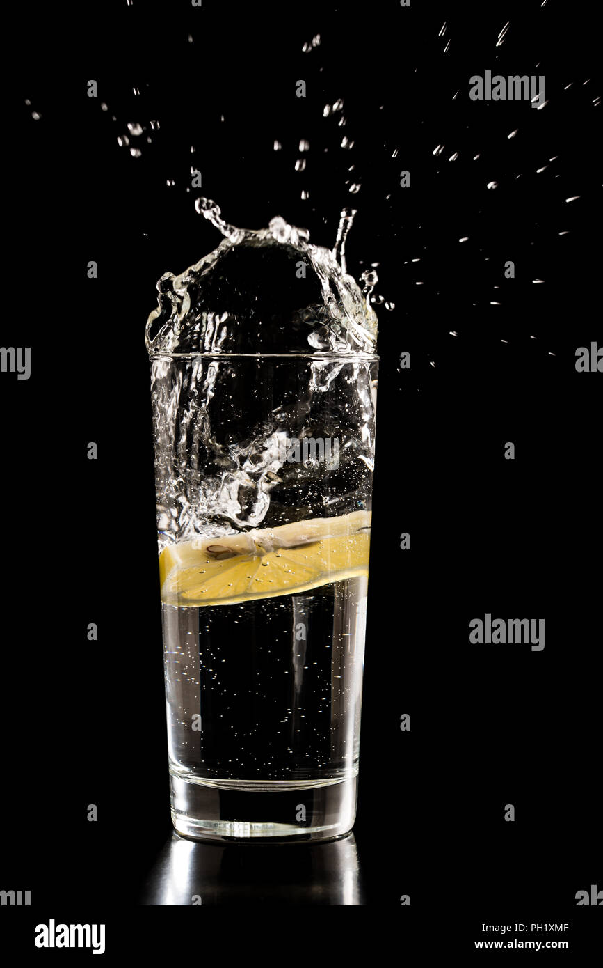 Slice of lemon splashing into a glass of water with a spray of water droplets in motion ...