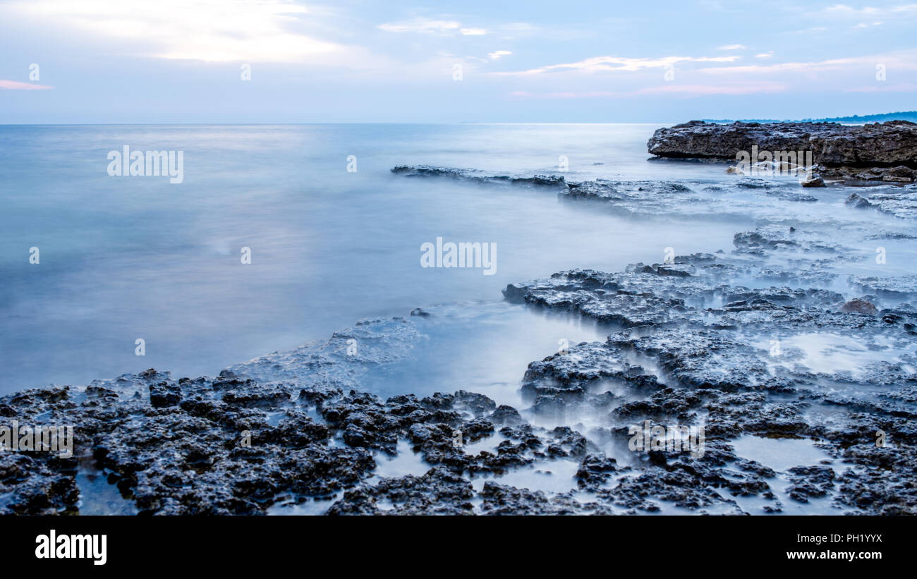 Rocky seashore and calm blue ocean under a cloudy sky with a shelf of ...