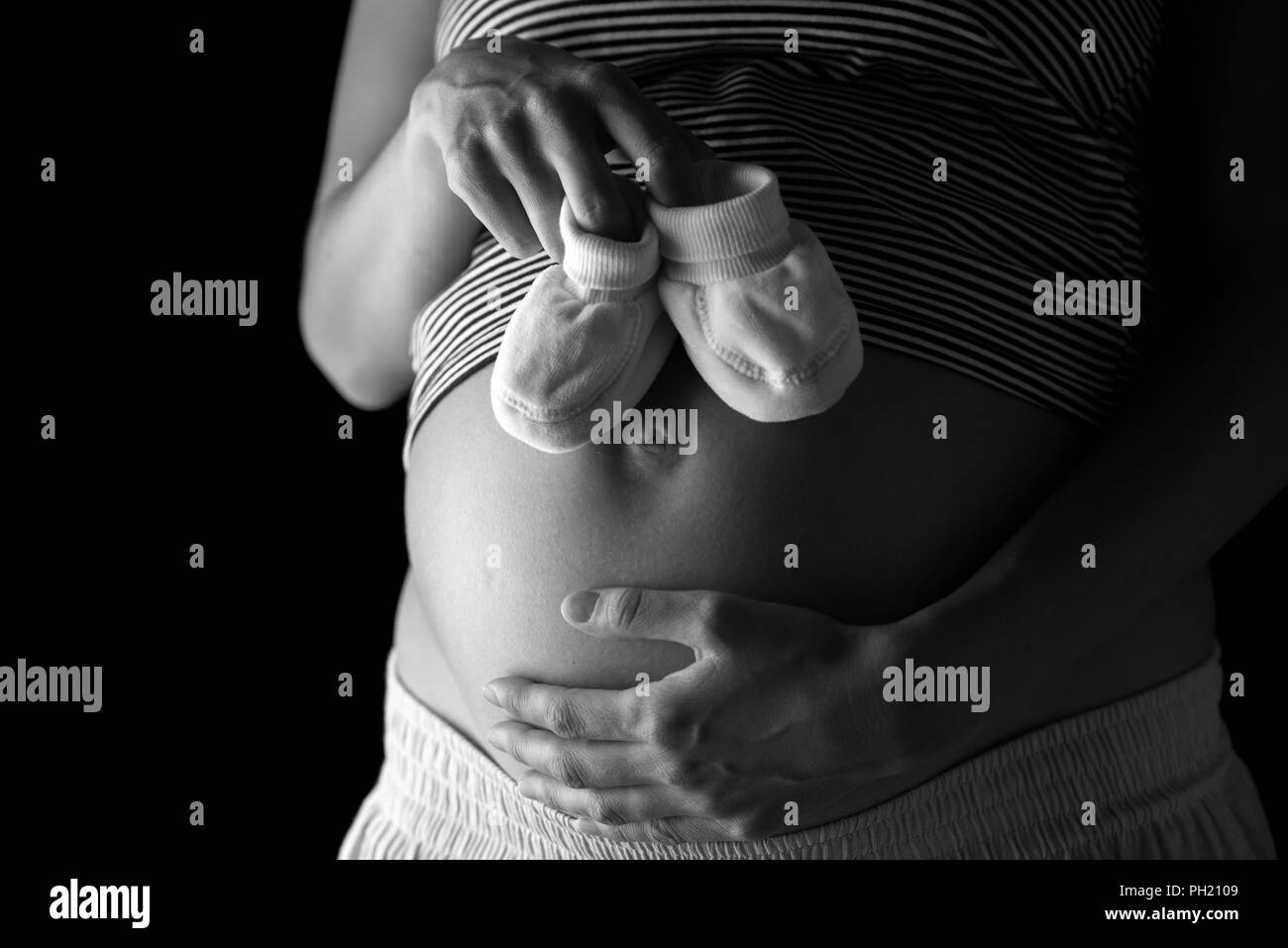 Pregnant woman holding a pair of cute baby booties above her swollen ...