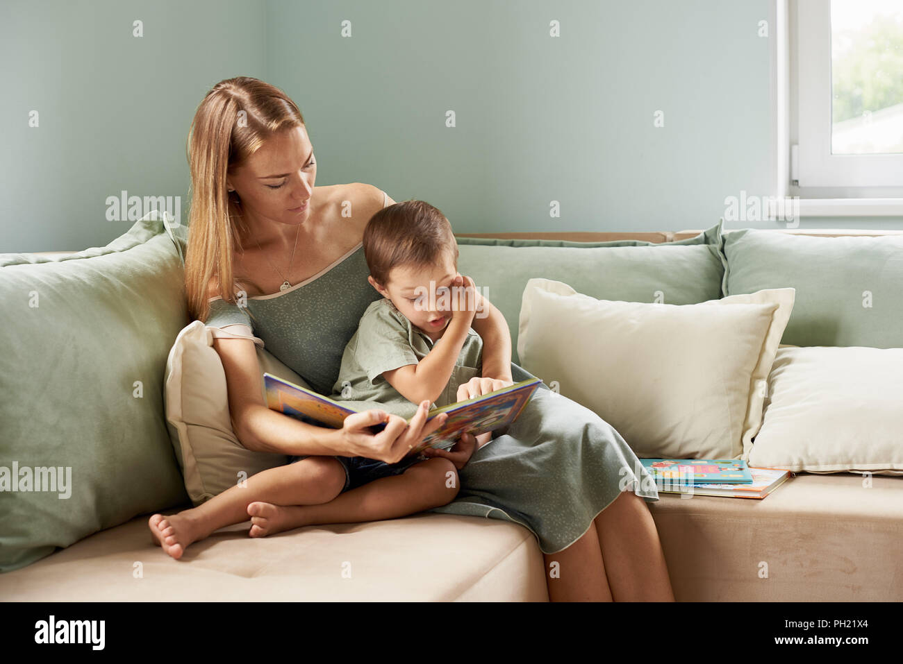 Young mother, read a book to her child, boy in the living room of their ...
