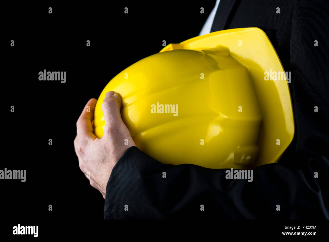 Close up view of a man in a suit holding a yellow hardhat under his arm ...