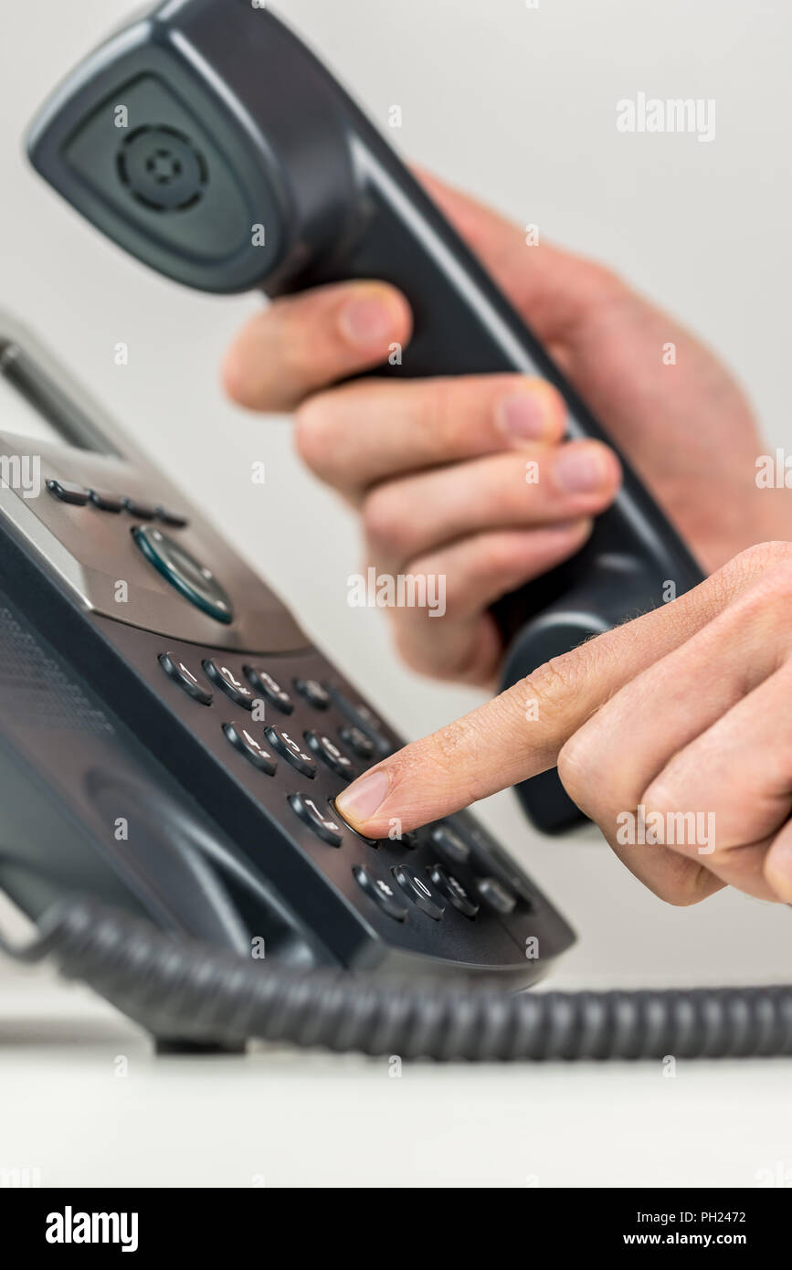 Close up view of the hands of a man dialing out on a landline telephone ...