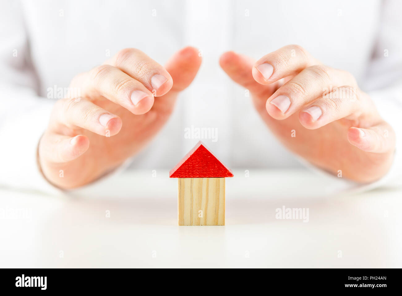 Male hands covering and protecting a small wooden model of a house or ...