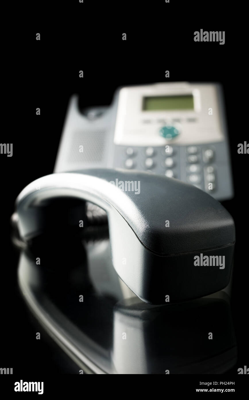 Landline telephone with receiver off the base on black desk with ...