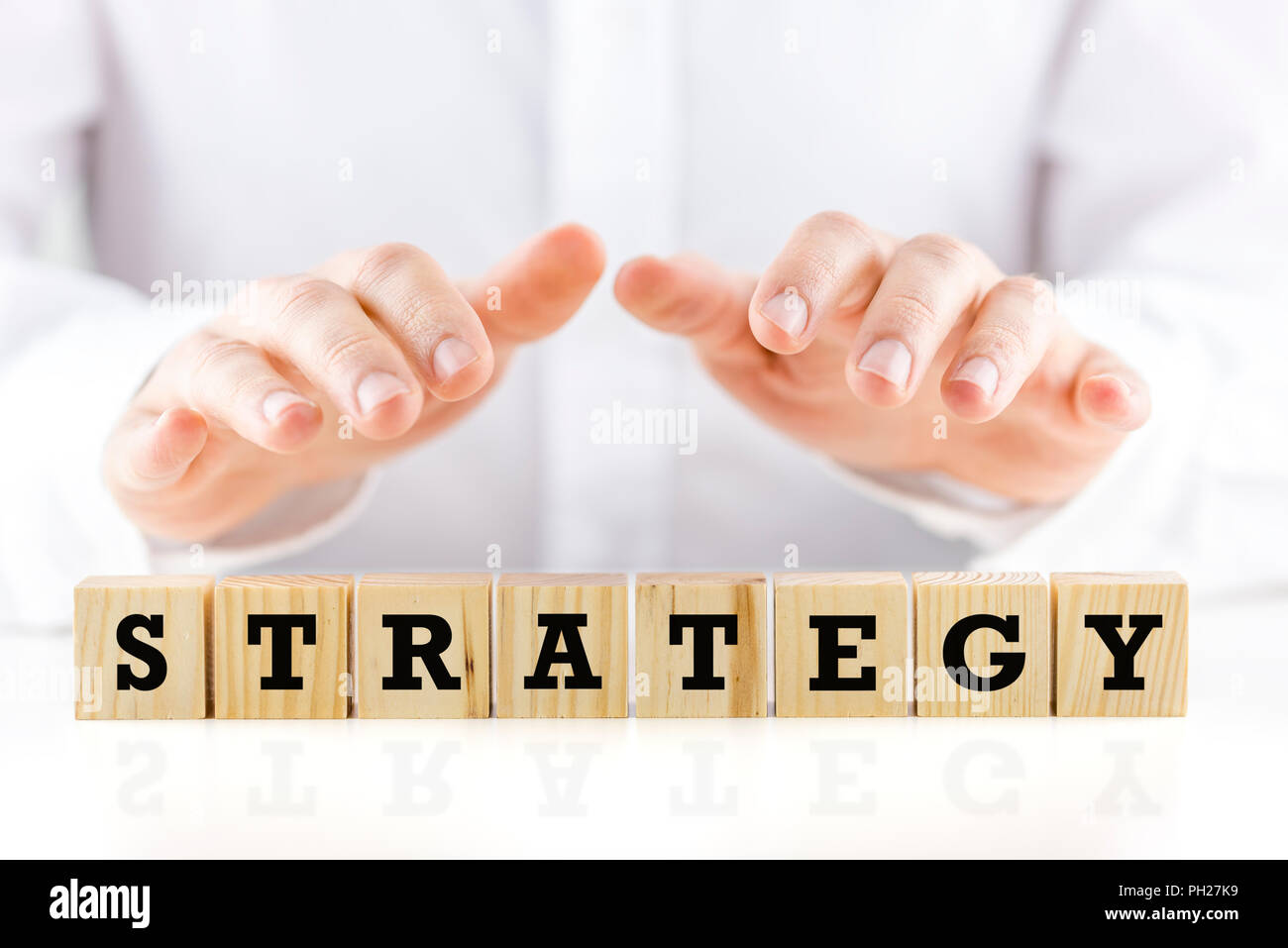 Man holding his hands protectively over the word Strategy on a row of ...