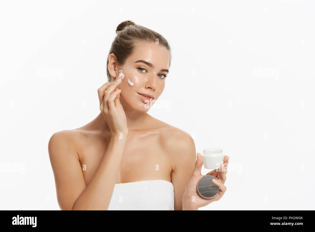 Beautiful young woman applying cosmetic cream treatment on her face isolated on white background ...